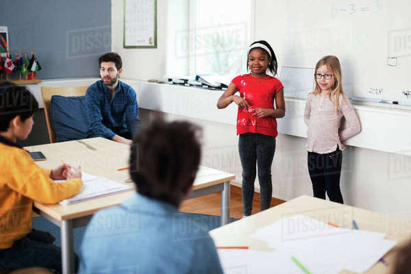 Female students standing against whiteboard wile teacher sitting in ...
