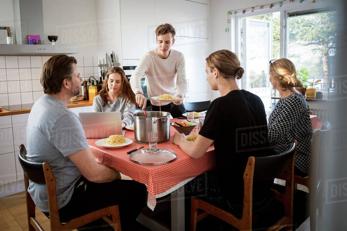 Man serving food for family at dining table - Stock Photo - Dissolve