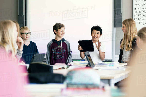 Happy boy giving presentation with digital tablet amidst students in ...