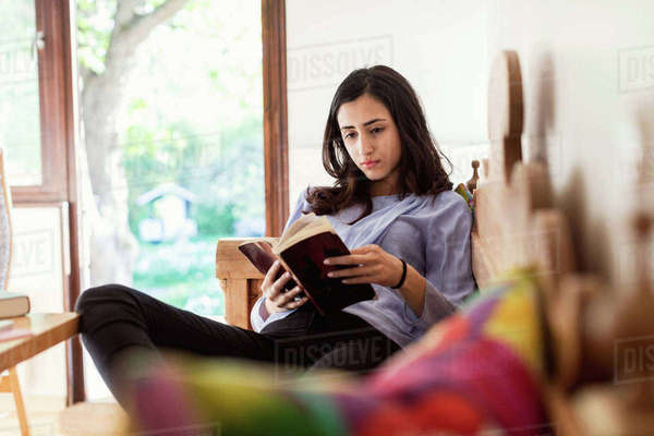 Teenage girl reading book while sitting on sofa - Royalty-free Stock ...