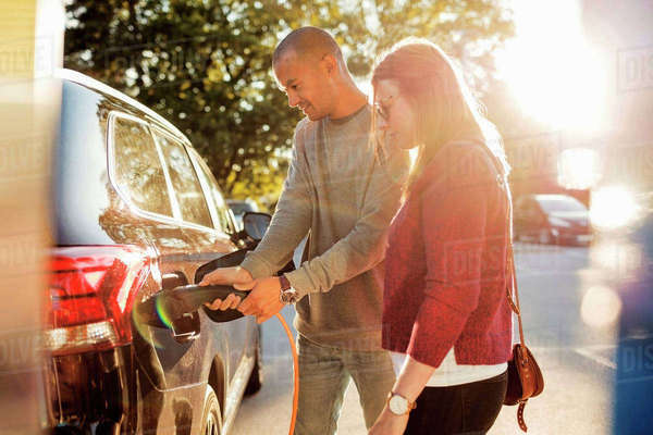 Couple charging electric car at station on sunny day - Royalty-free ...