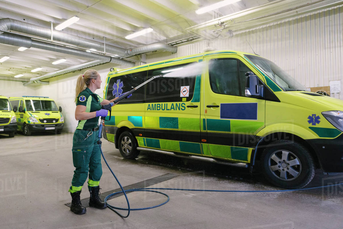 Full length of female paramedic washing ambulance at parking lot ...