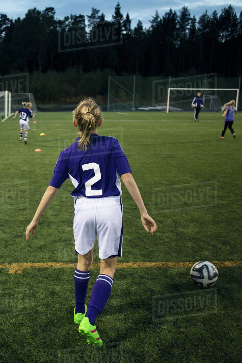 Rear view of girl playing with soccer ball on field - Royalty-free ...