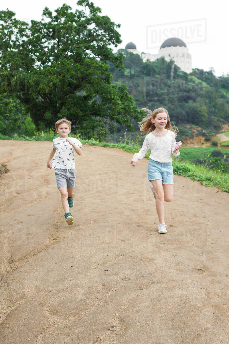Full length of brother and sister running on dirt road - Stock Photo ...