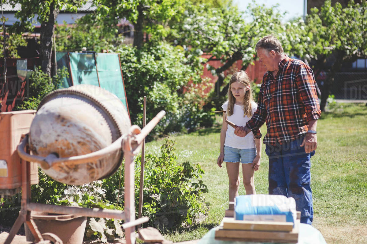 Grandfather giving shovel to granddaughter while standing by cement ...