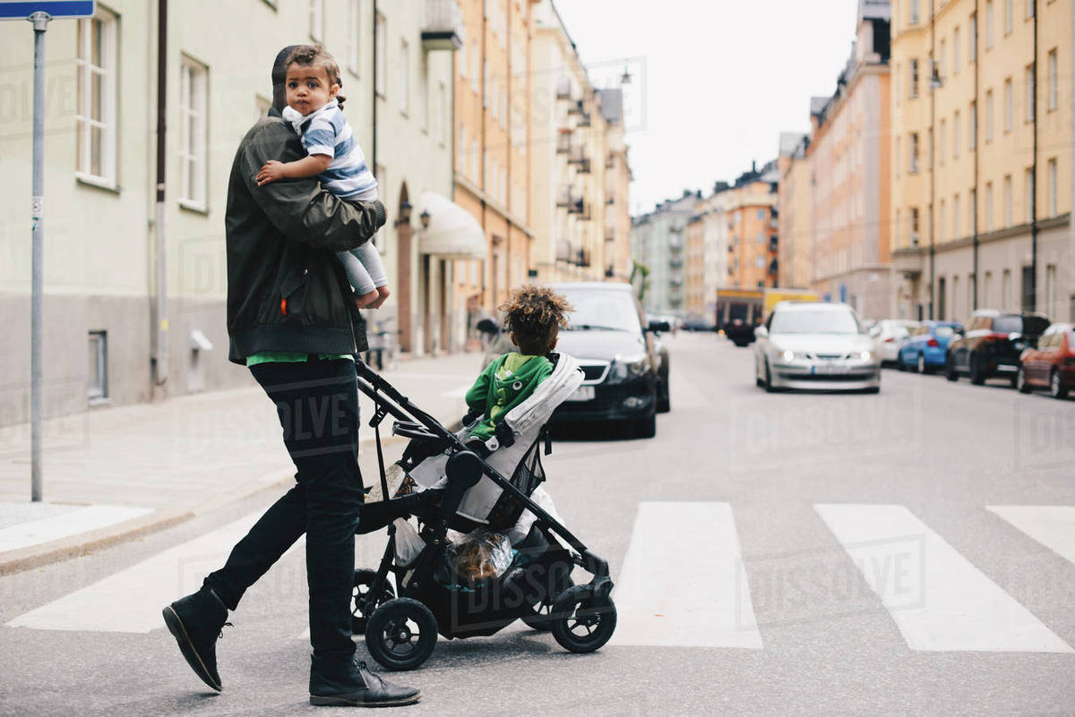 Father crossing road with children while pushing baby stroller in city ...