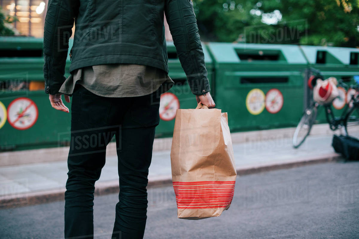 Midsection of man carrying paper bag against garbage cans - Royalty ...