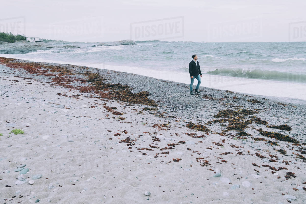 Full length of young man walking by sea at beach - Stock Photo - Dissolve