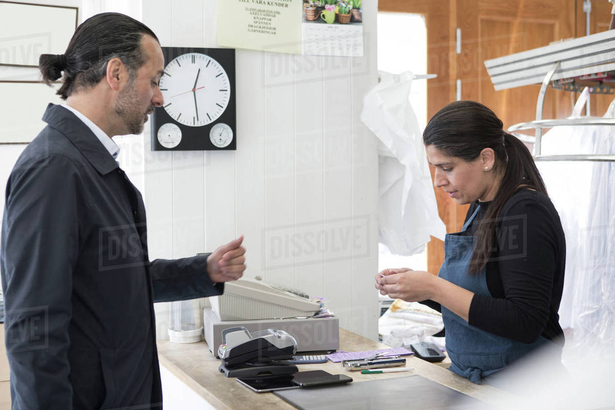 Side view of mature male customer standing at checkout with owner ...