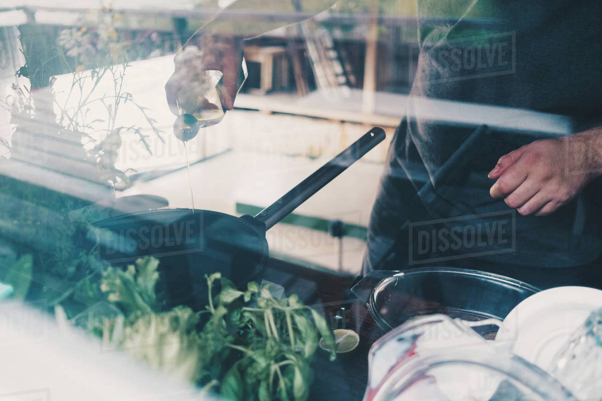 Midsection of man cooking food seen through glass window with ...