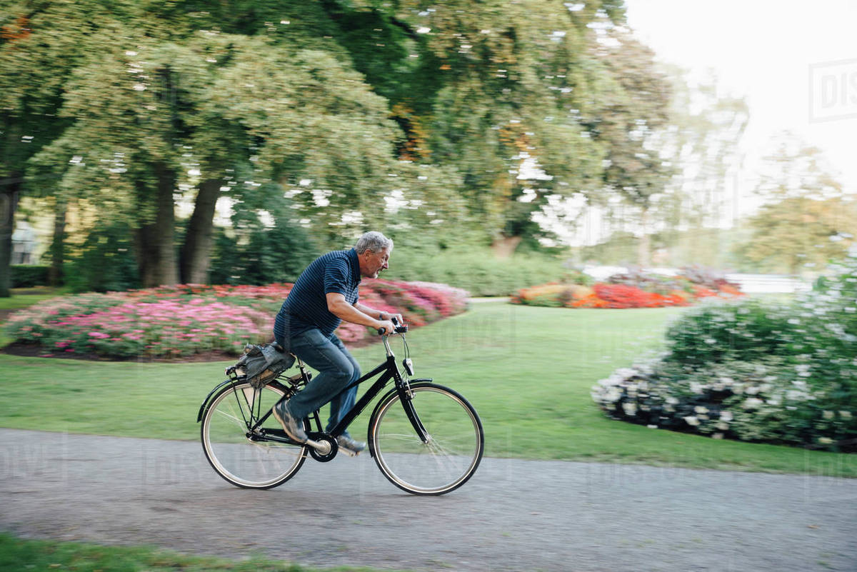 Full length side view of senior man riding bicycle in park - Stock ...