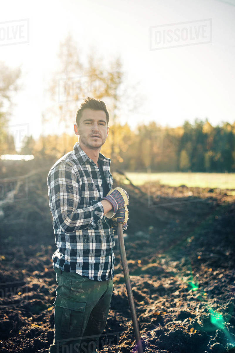 Portrait of confident male farmer with shovel standing on organic farm ...