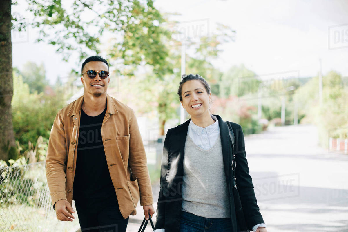Portrait of smiling friends talking while walking on street in city ...