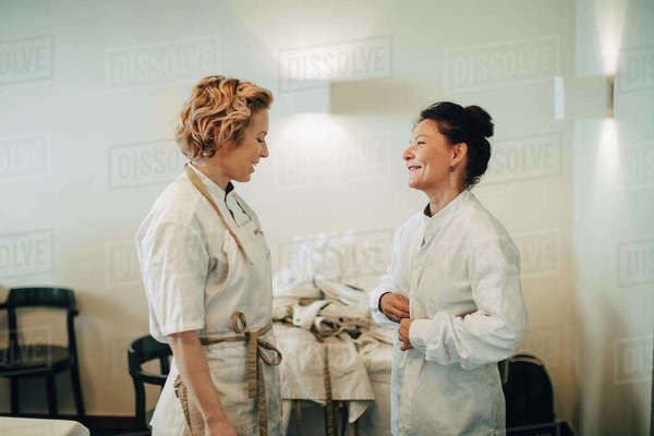 Cheerful female restaurant owners talking while standing against wall ...
