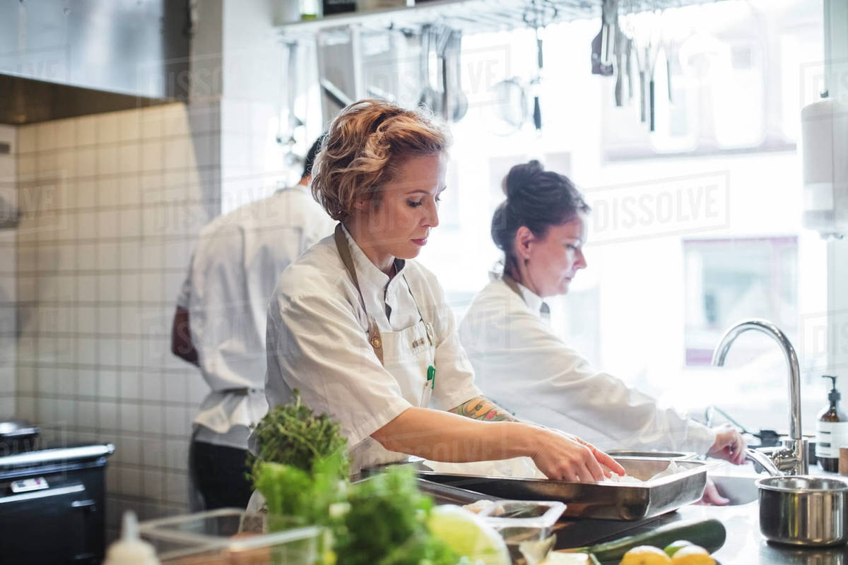 Female chefs preparing food on counter by colleagues in kitchen at ...