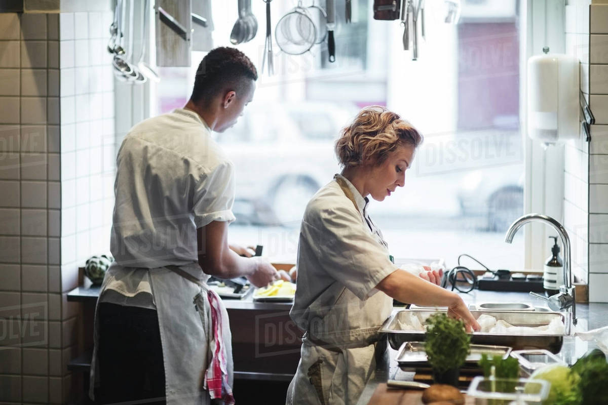 Side view of female chef preparing food on counter in kitchen with male ...