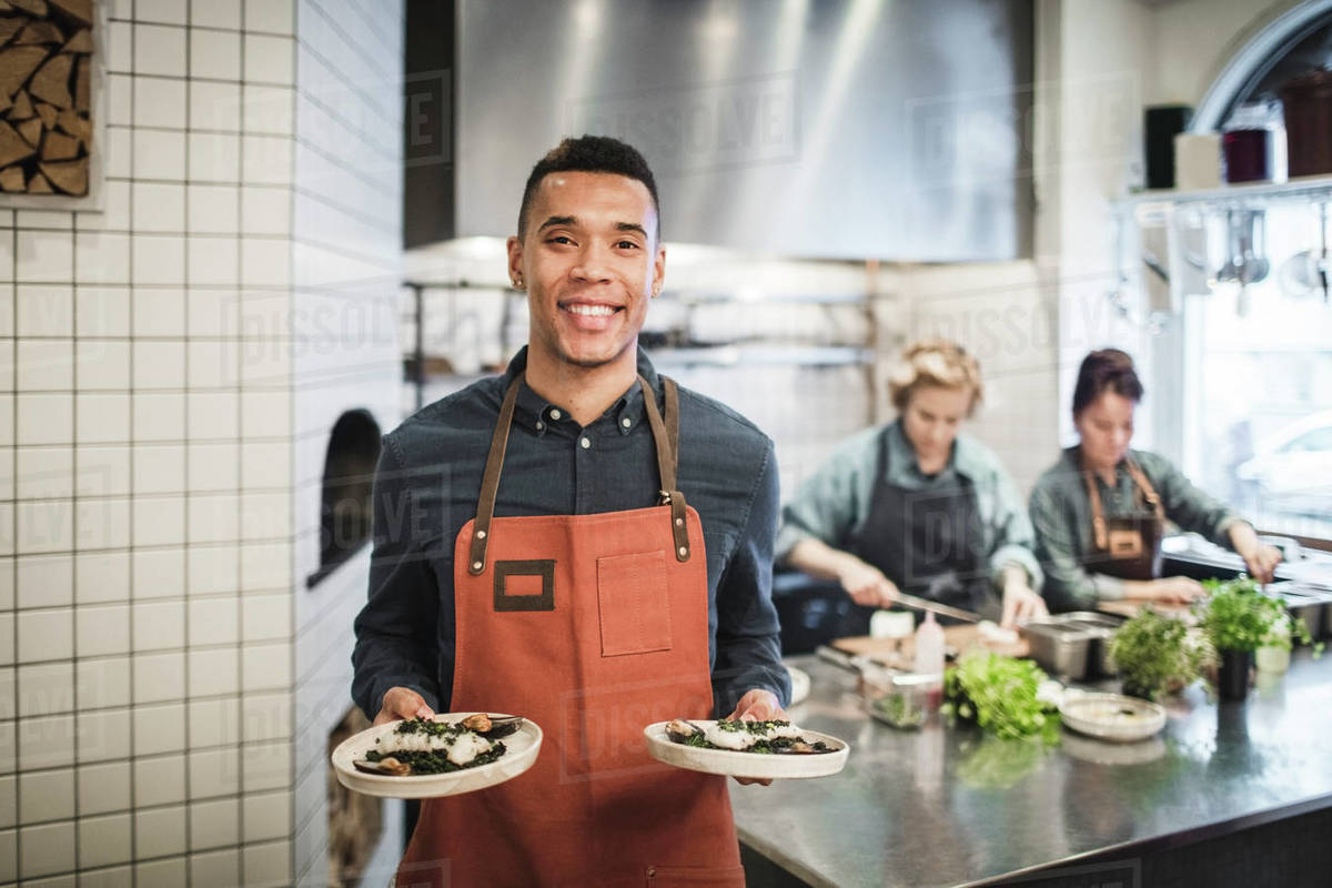 Portrait of smiling waiter holding fresh food plates against female ...