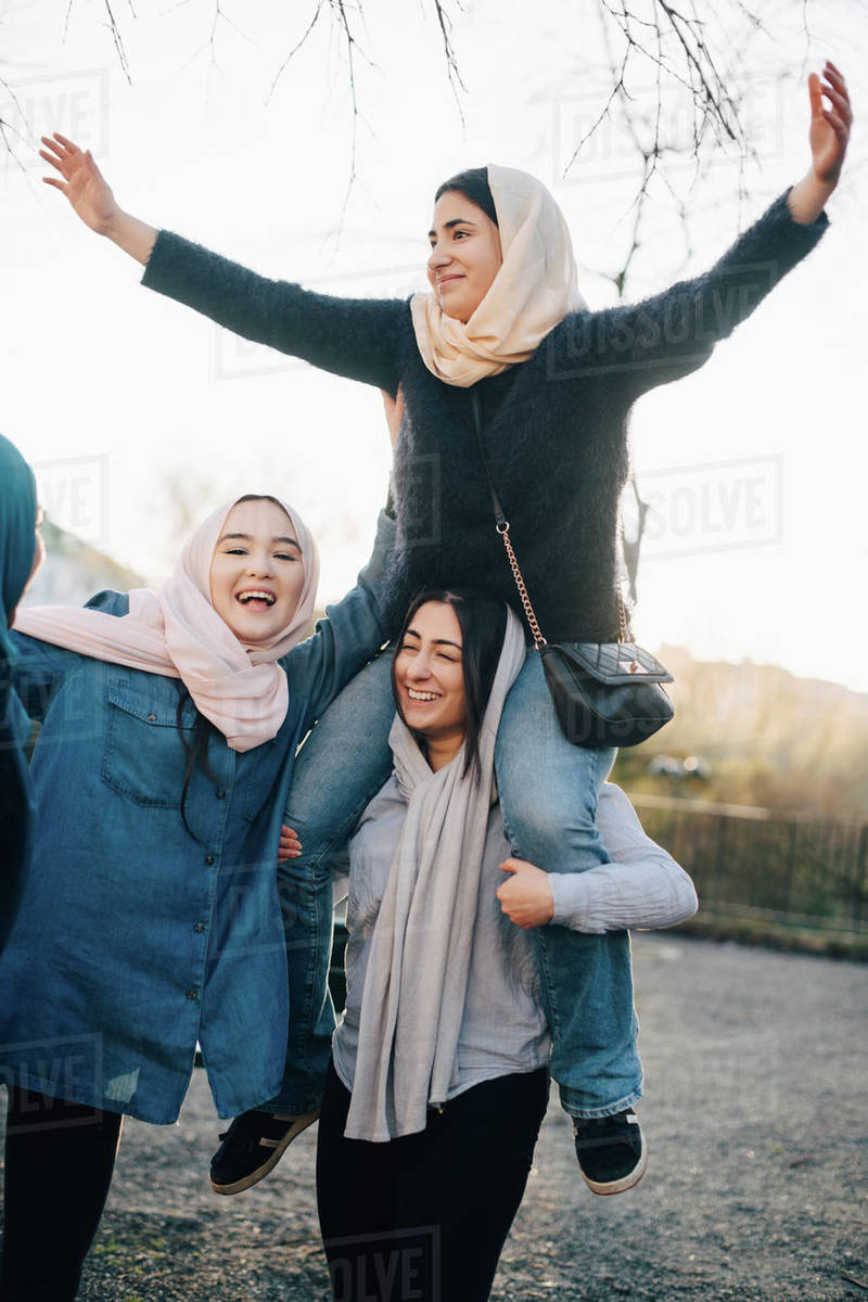 Young woman carrying teenage girl on shoulders by friends against clear ...