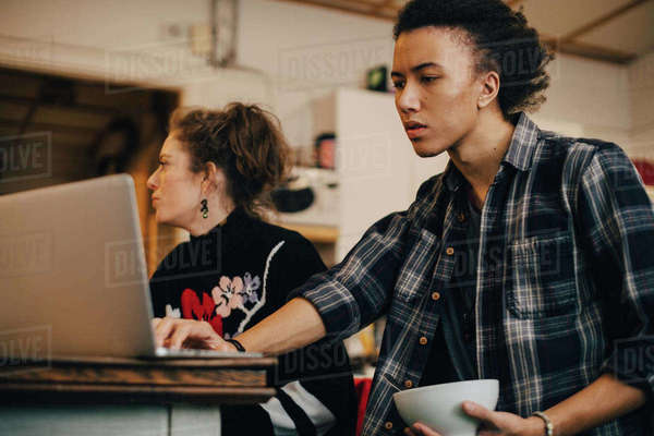 Young businessman using laptop while sitting with female colleague at ...