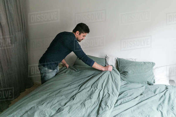 High angle view of man making bed while standing in bedroom at home ...