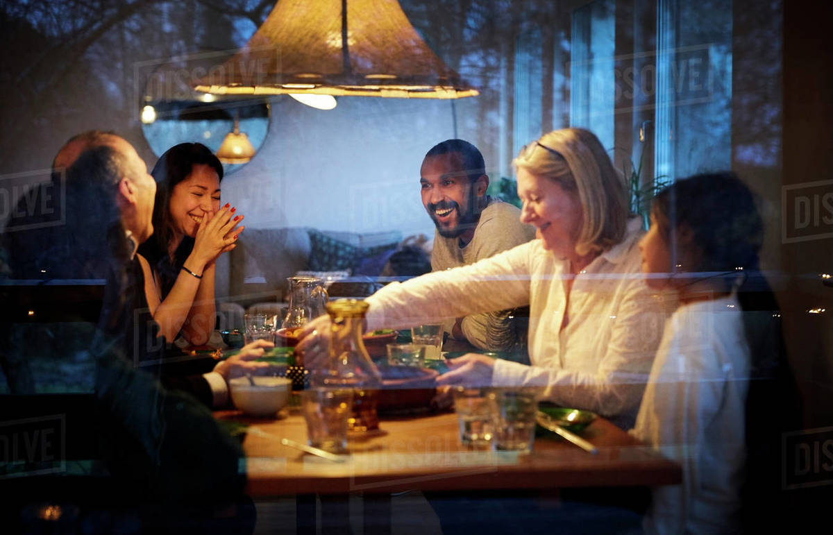 Happy family enjoying while having dinner at table seen through glass ...