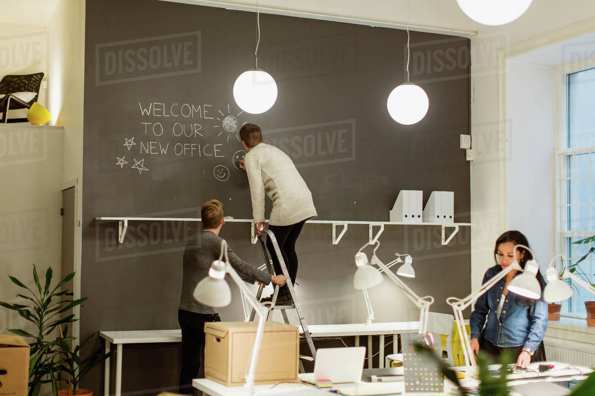 Businesswoman standing on step ladder drawing smiley face on wall while ...