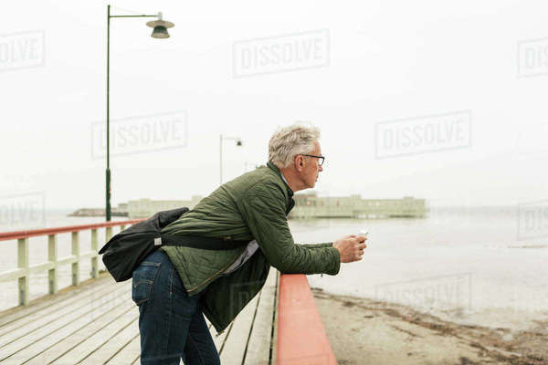Side view of senior man leaning on railing while looking at sea against ...