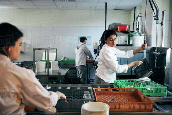 Female chef washing dishes in commercial kitchen - Stock Photo - Dissolve
