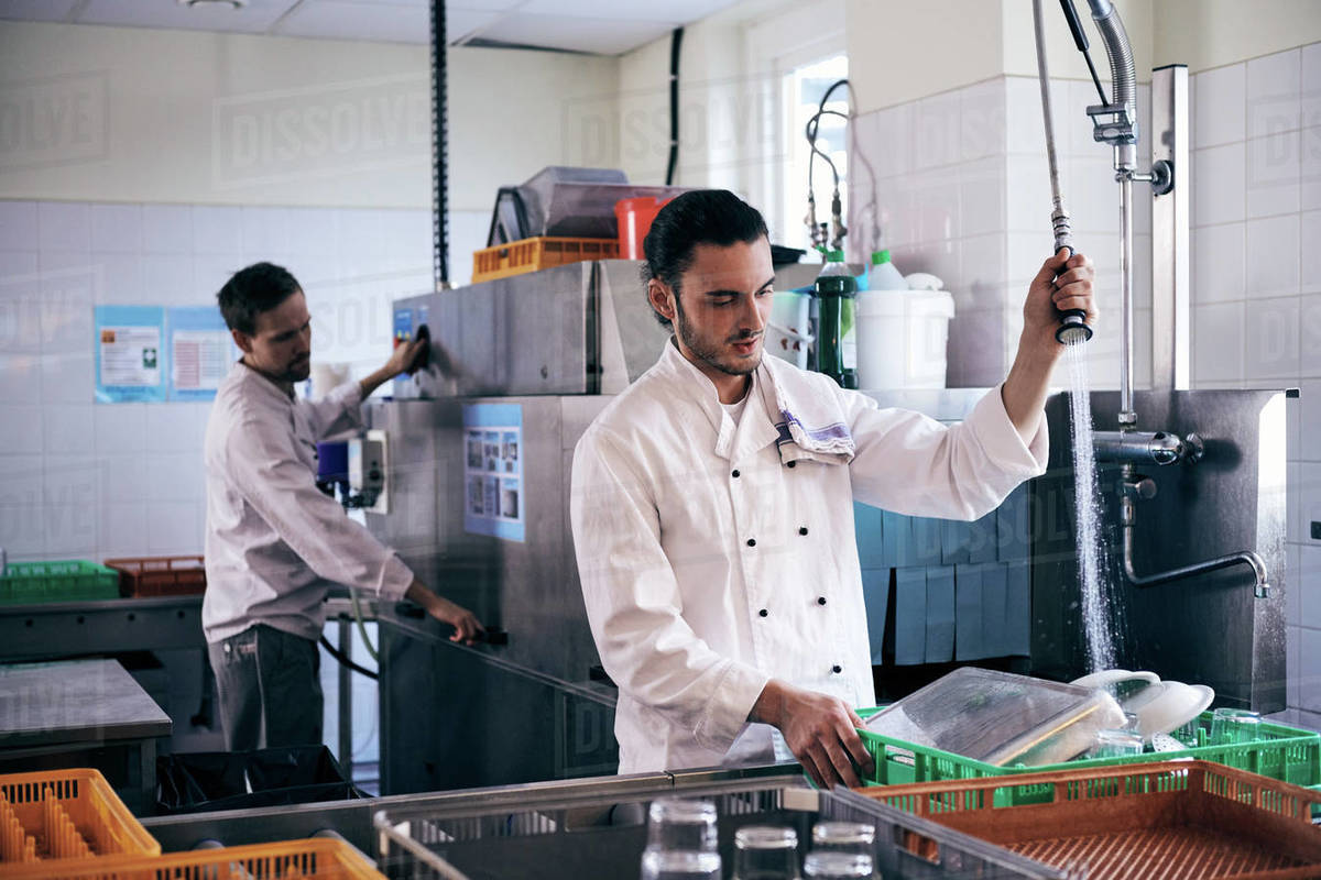 Chef spraying water on plates while colleague working in commercial ...