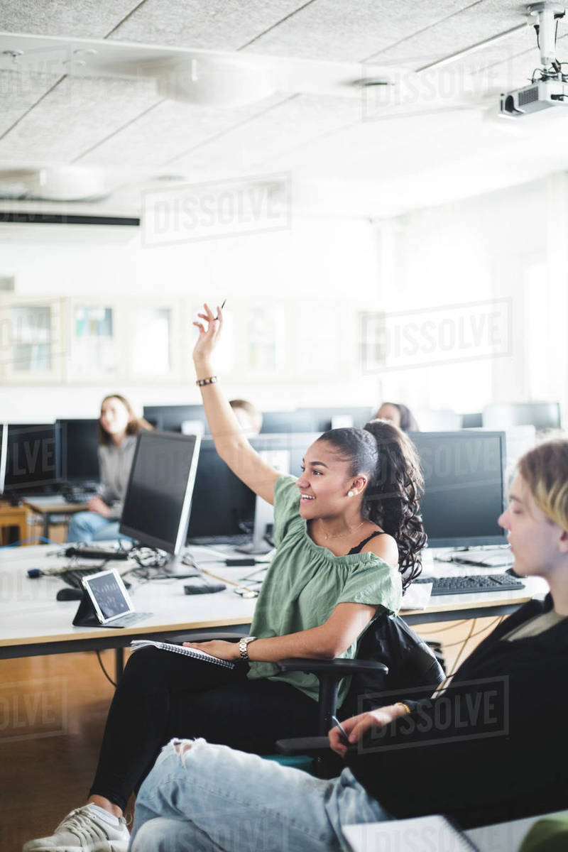 Smiling teenage girl sitting with hand raised by young friend in ...