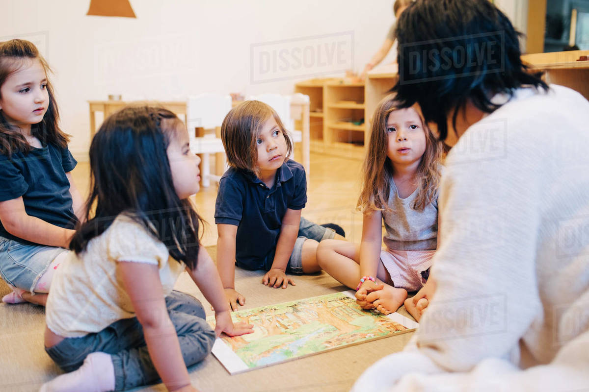 Female teacher telling story to students sitting in classroom at child ...