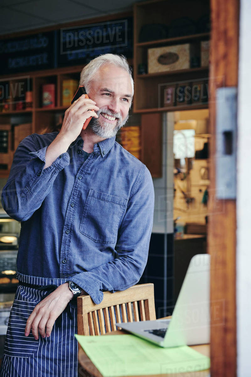 Sales clerk smiling while talking on mobile phone in deli - Royalty ...