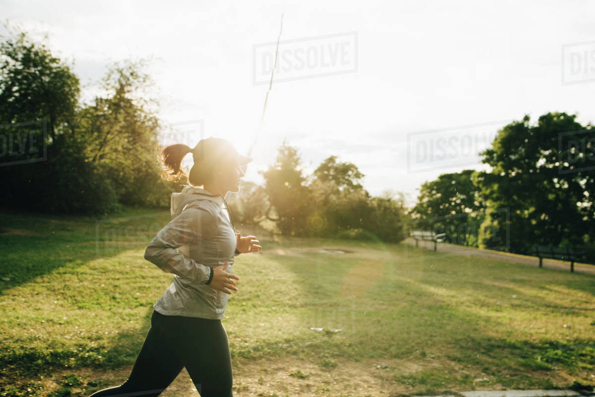 Side view of female athlete jogging at park during sunny day - Royalty ...