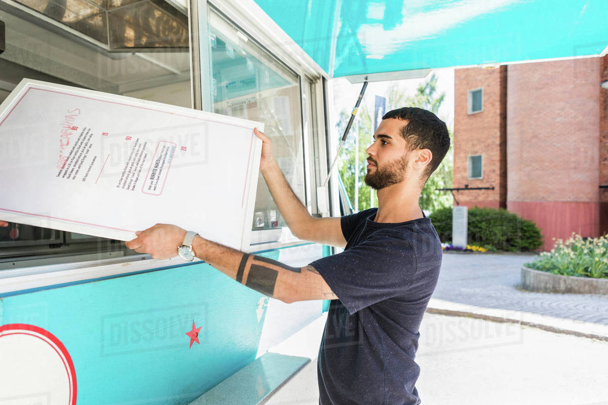 Side view of confident young male salesman holding menu placard at food ...