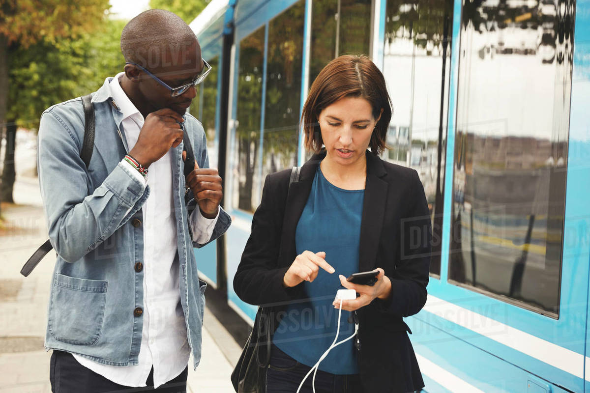 Multi-ethnic commuters discussing over smart phone while standing blue ...
