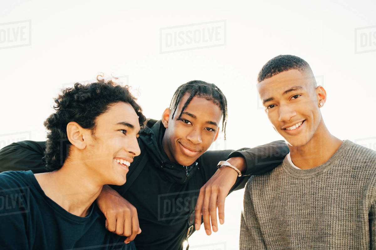 Portrait of smiling teenage boys with friend against clear sky ...