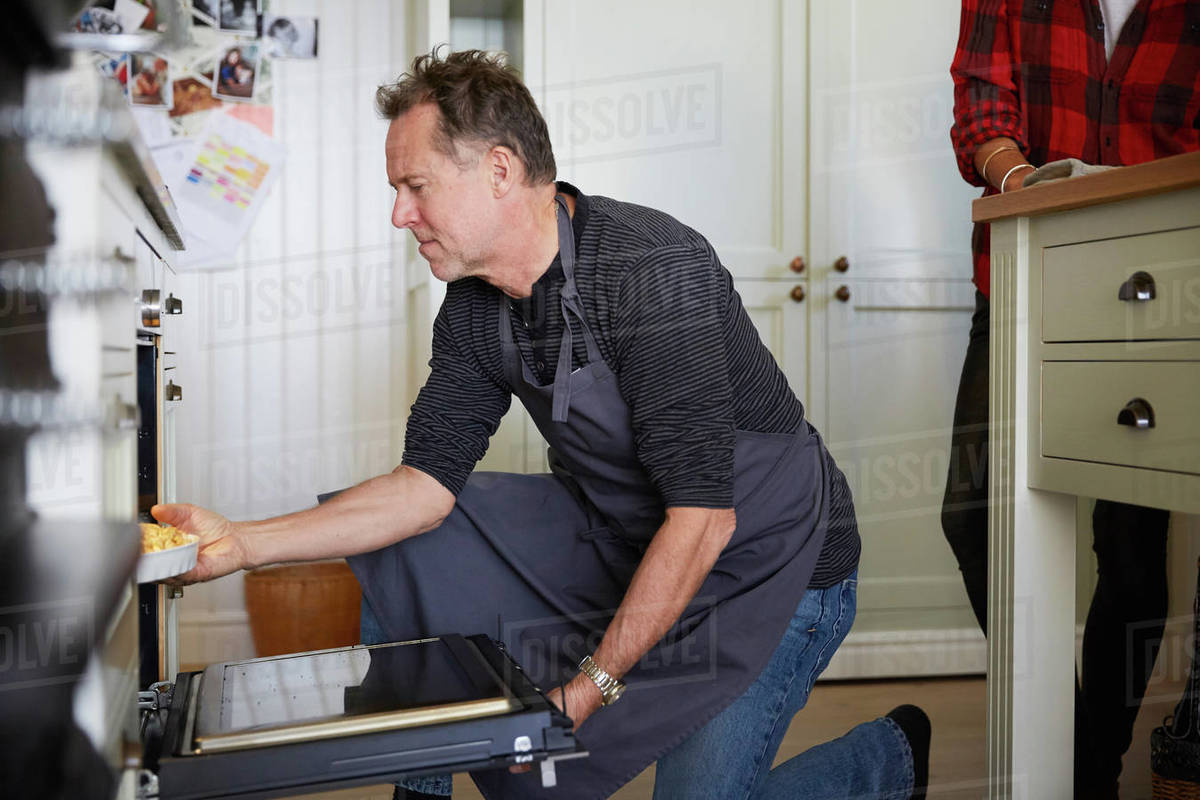 Side view of mature man inserting food in oven at home - Stock Photo ...