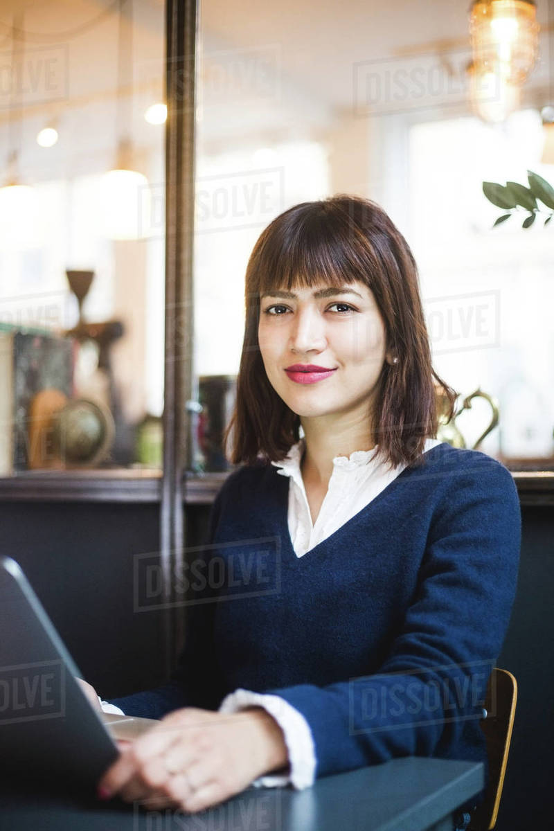 Portrait of confident female professional sitting with laptop at office ...