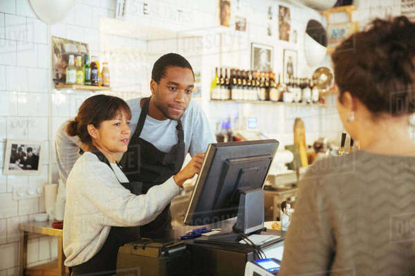 Young employee standing by female cashier using computer with customer ...