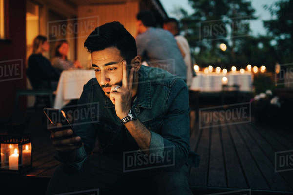 Man using mobile phone while friends in background during dinner party ...