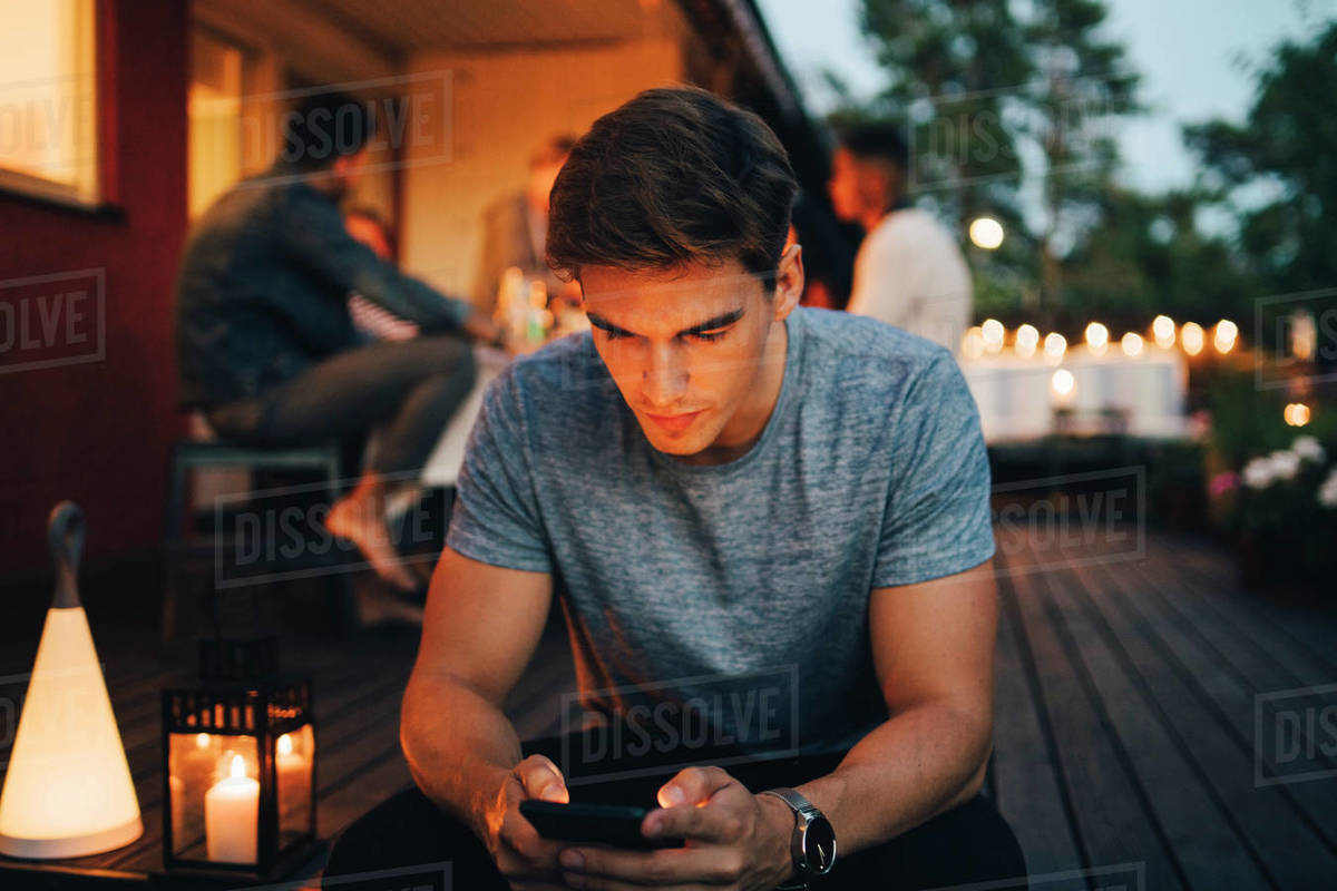 Young man using smart phone while friends in background during dinner ...