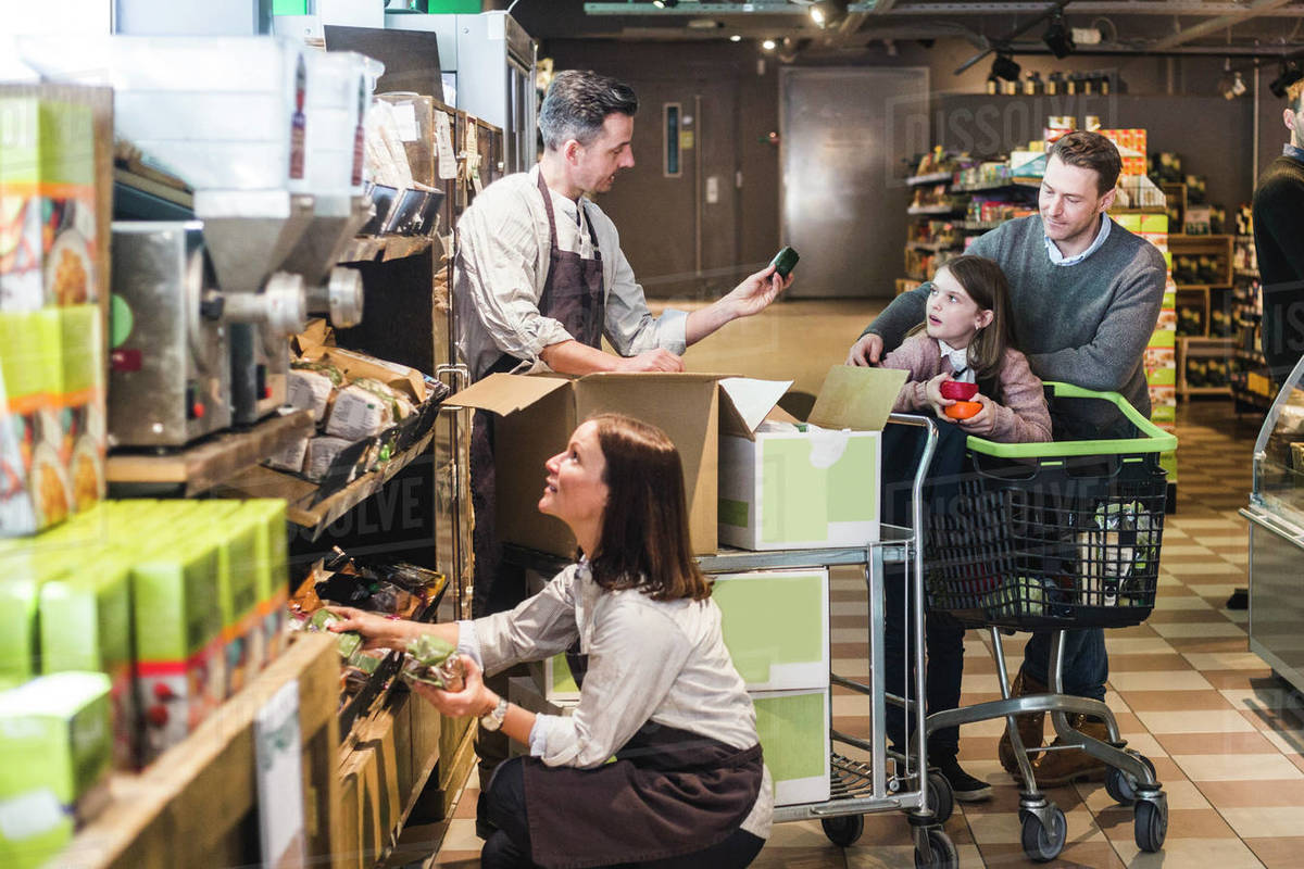 Salesman assisting customers while saleswoman arranging shelf in ...