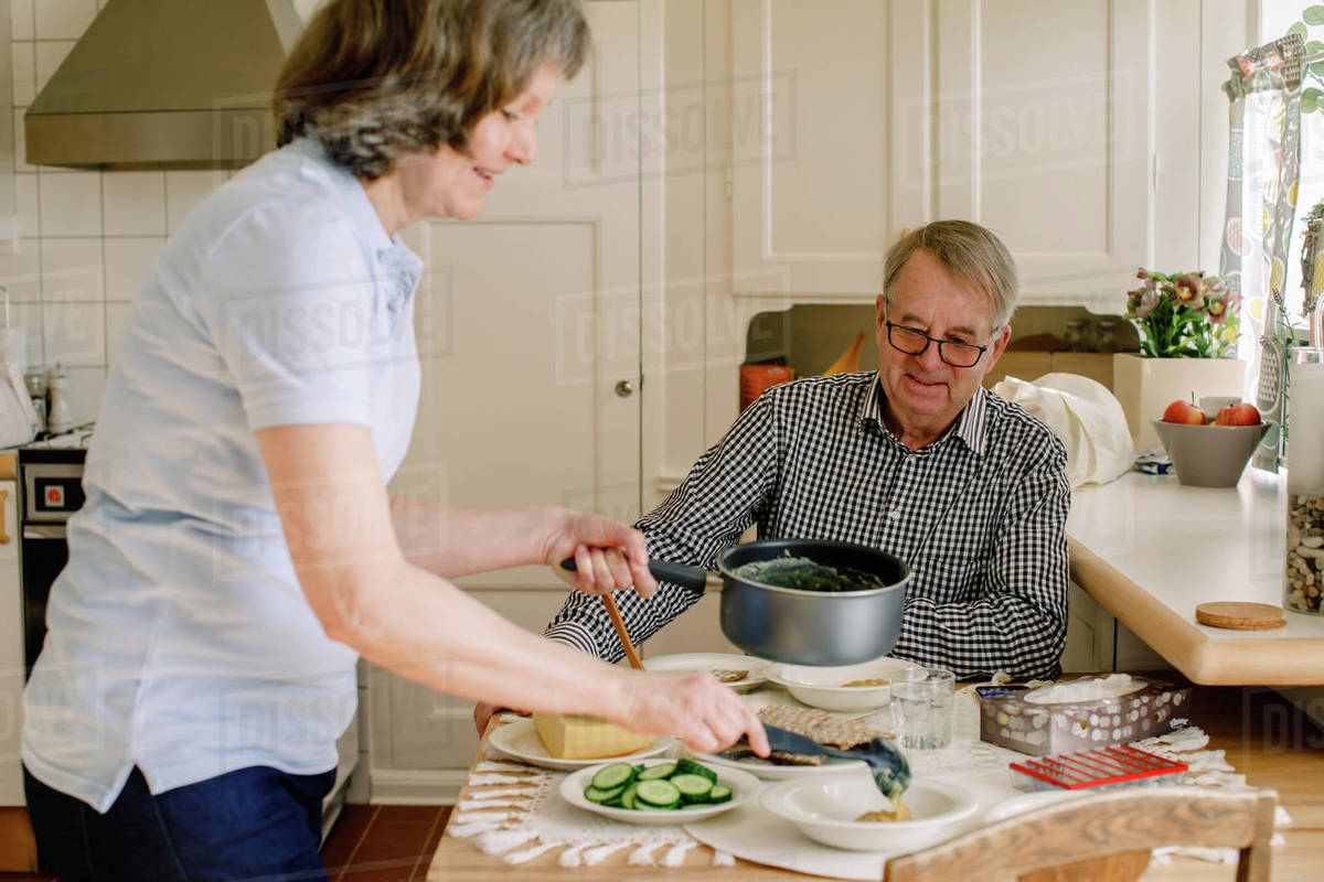 Side view of female caregiver is serving meal at table for retired ...