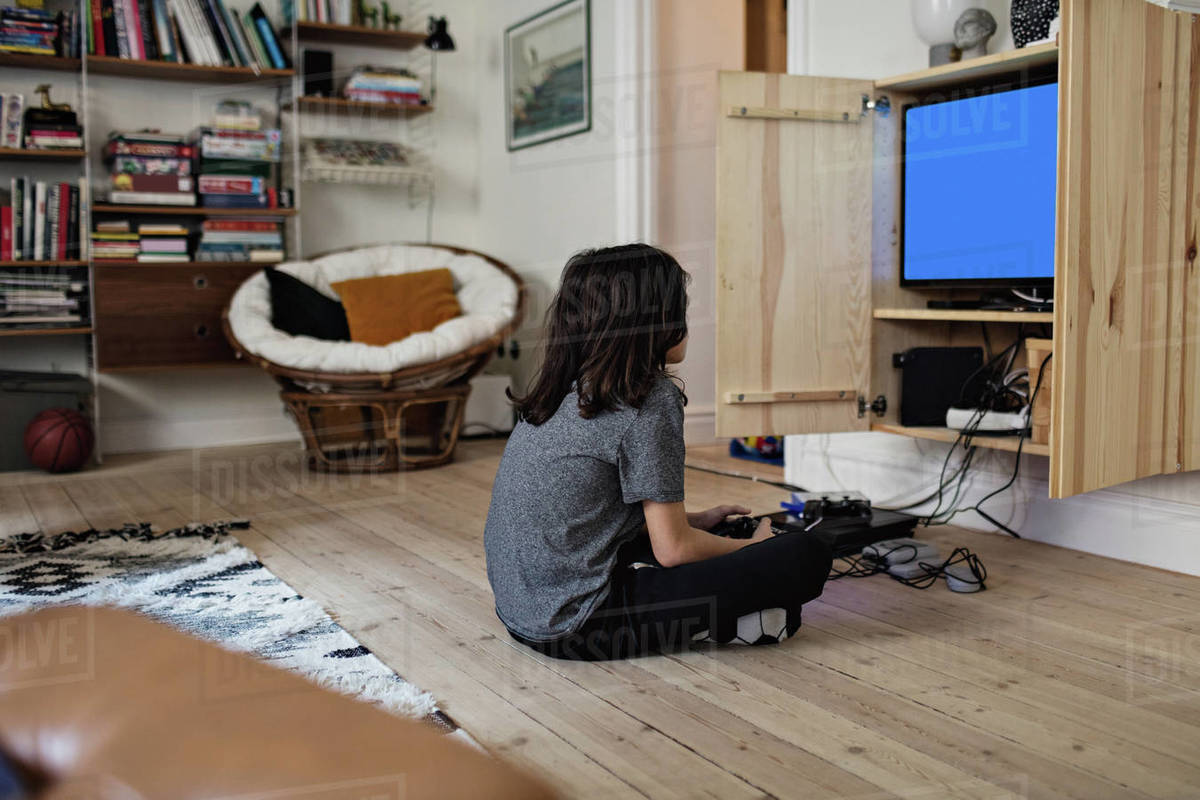 Side view of boy playing video game while sitting on hardwood floor at ...