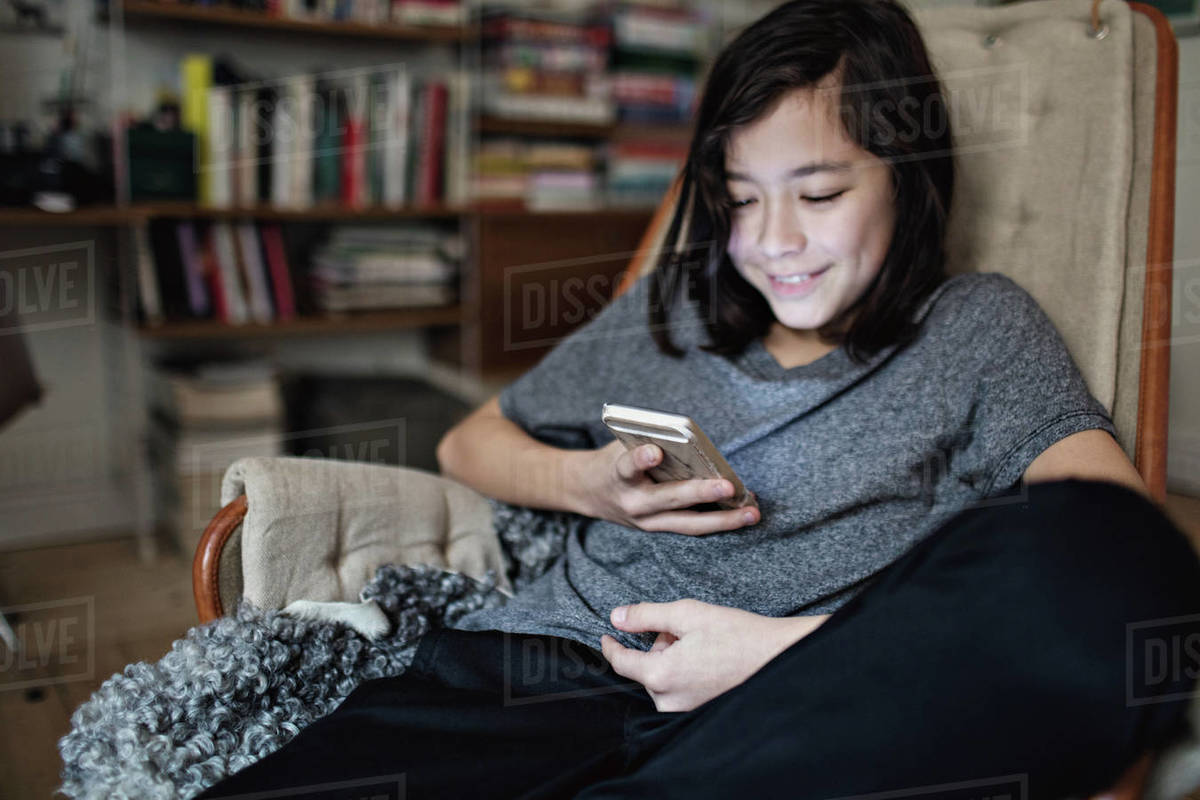 Smiling boy using social media on smart phone while sitting at home ...