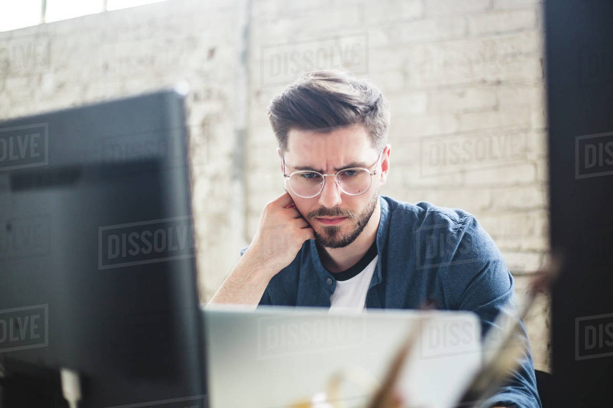 Male IT professional thinking while working on computer codes in laptop ...
