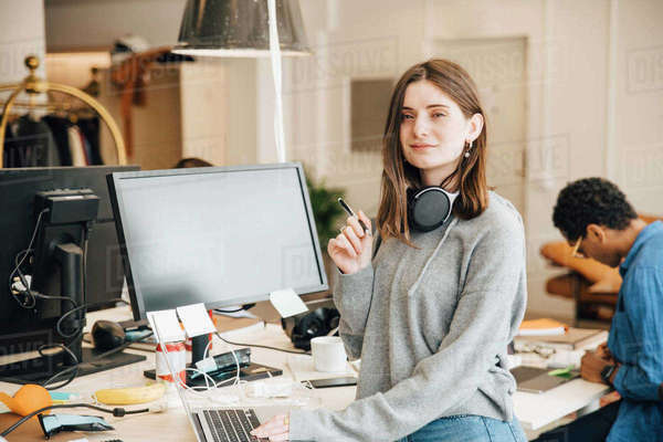 Portrait of smiling female computer programmer using laptop at desk in ...