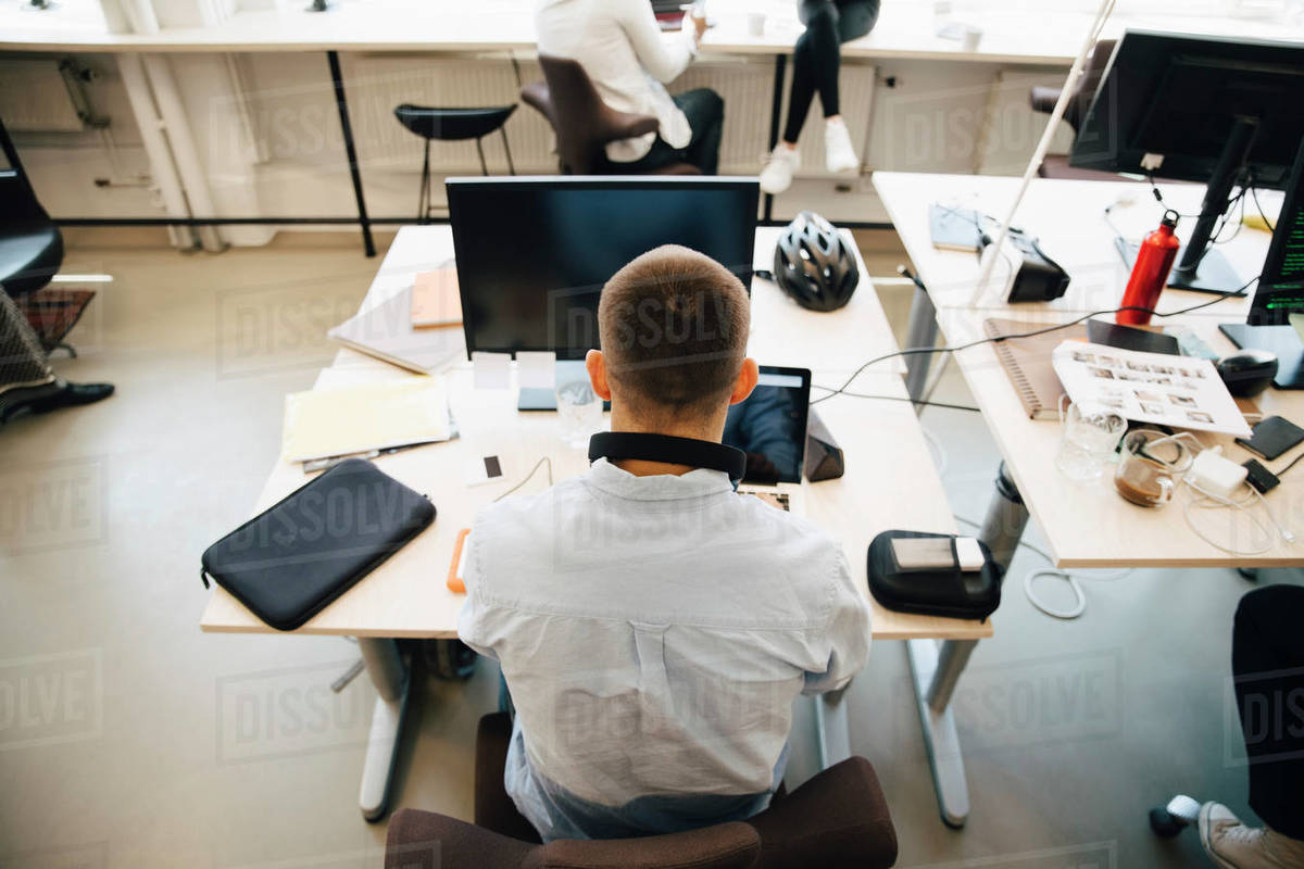 Rear view of male computer programmer using laptop on desk while ...