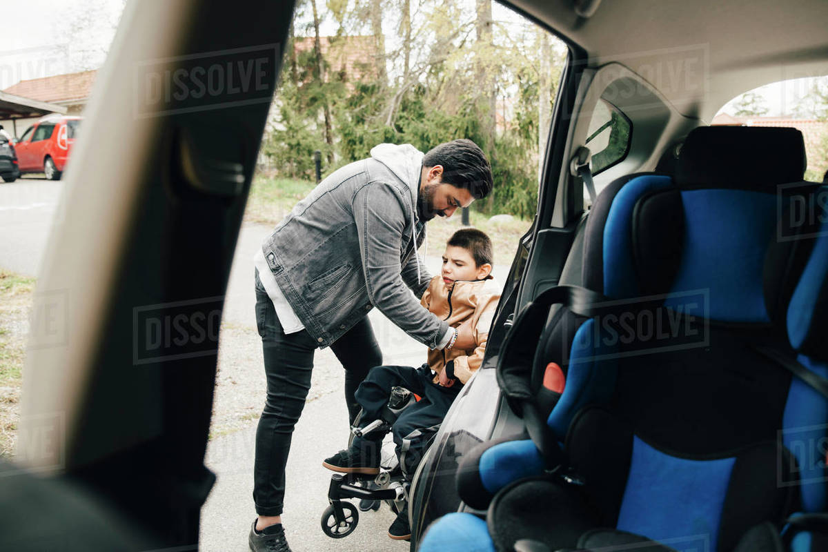 Father carrying disabled son from wheelchair seen from car - Stock ...