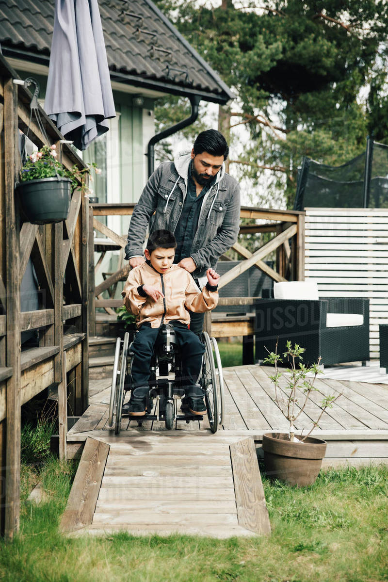 Father pushing autistic son sitting on wheelchair in yard - Royalty ...